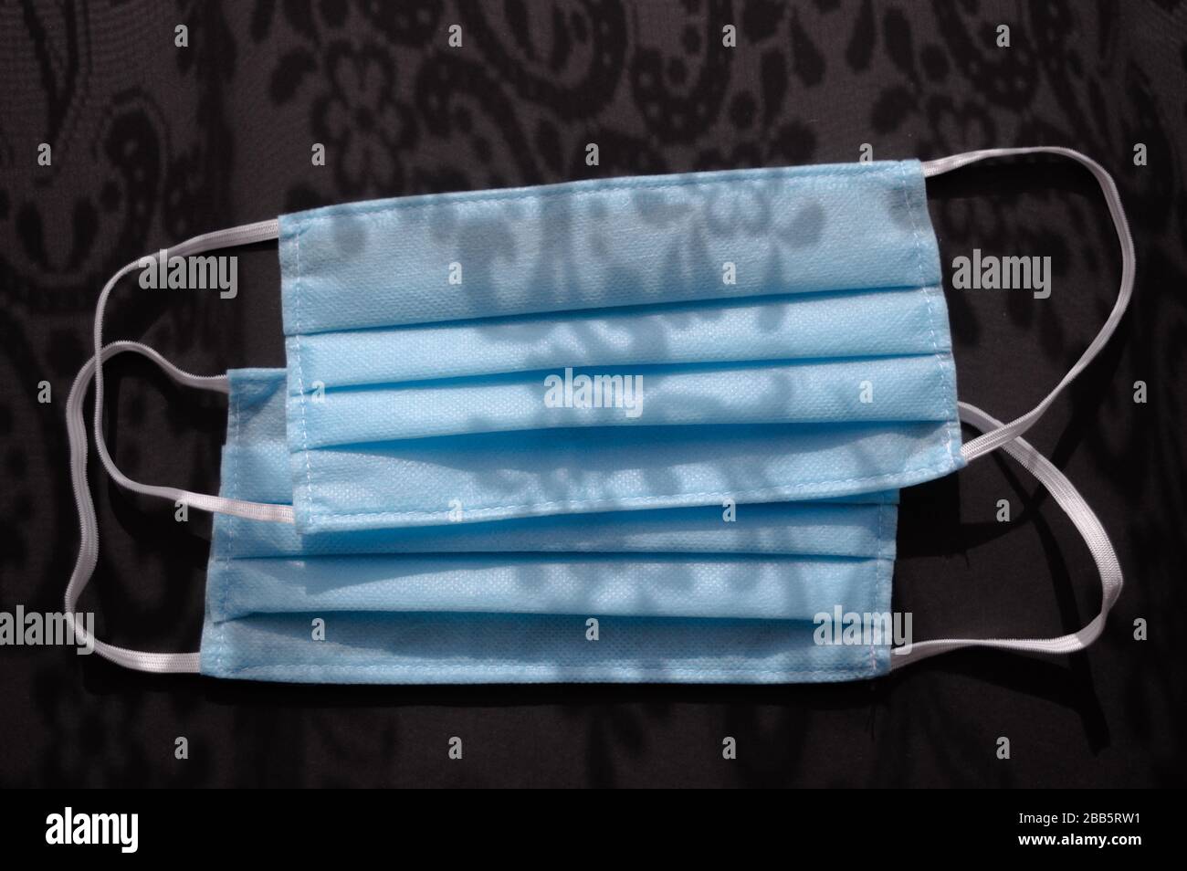 Two light blue medical disposable face masks on the dark black ...