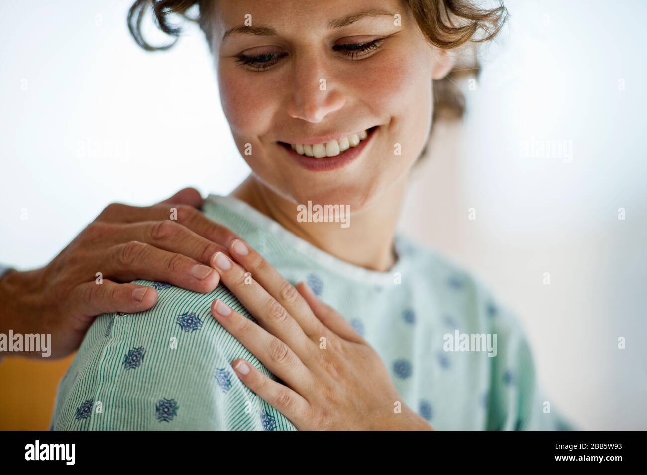 Female Hospital Patient Smiling As She Touches The Comforting Hand Laid