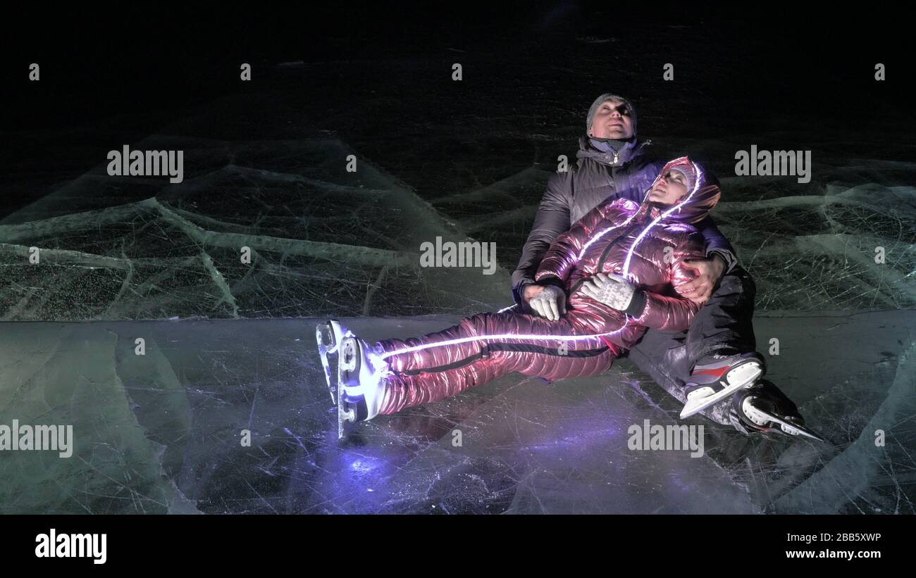 Young loving couple skating at ice rink at night. Man and woman kiss ...