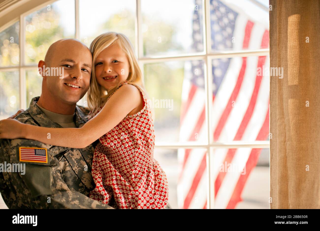 Portrait of a happy soldier hugging his young daughter inside their ...