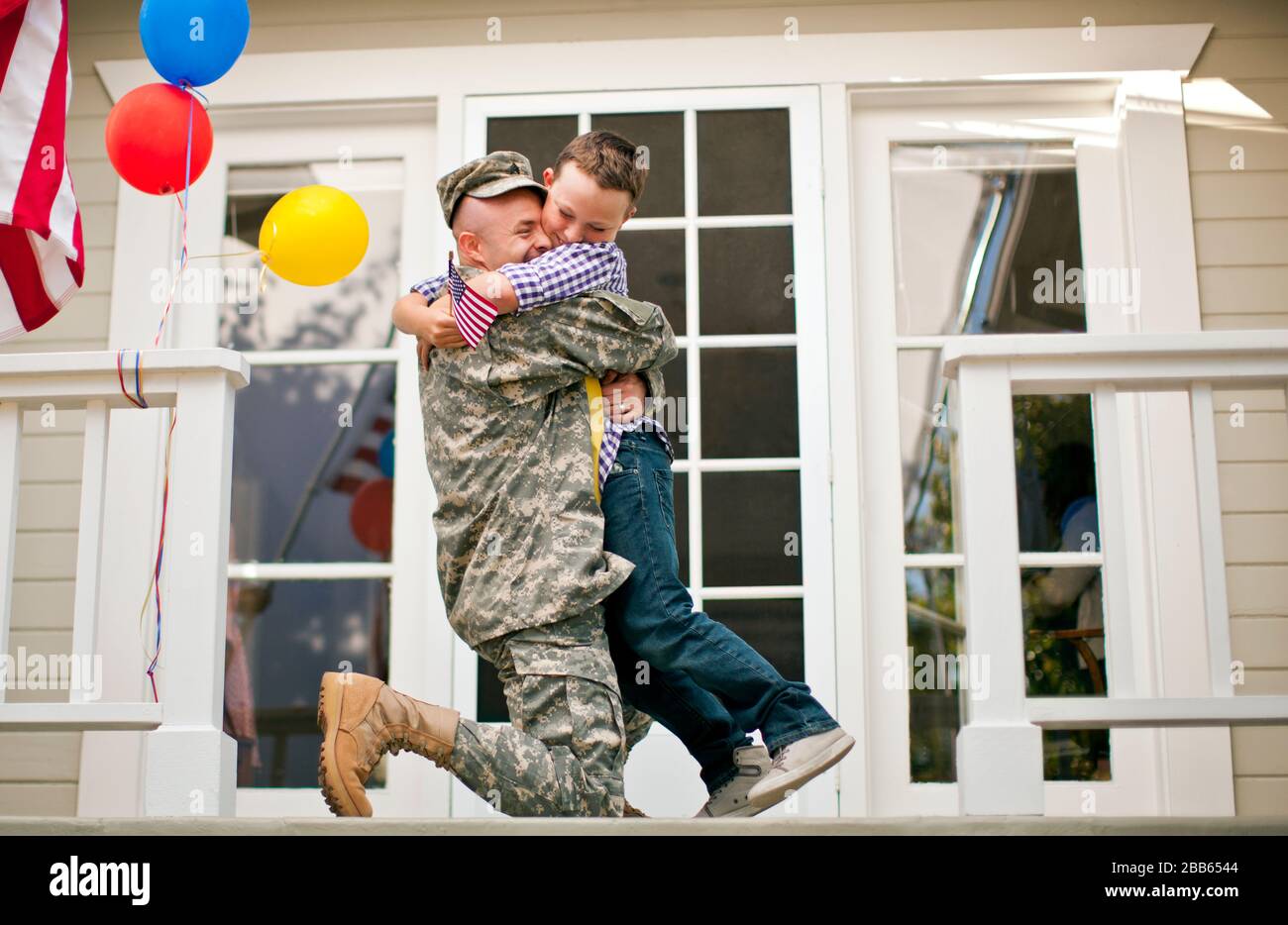 Happy army soldier hugging his young son on the porch of their home ...