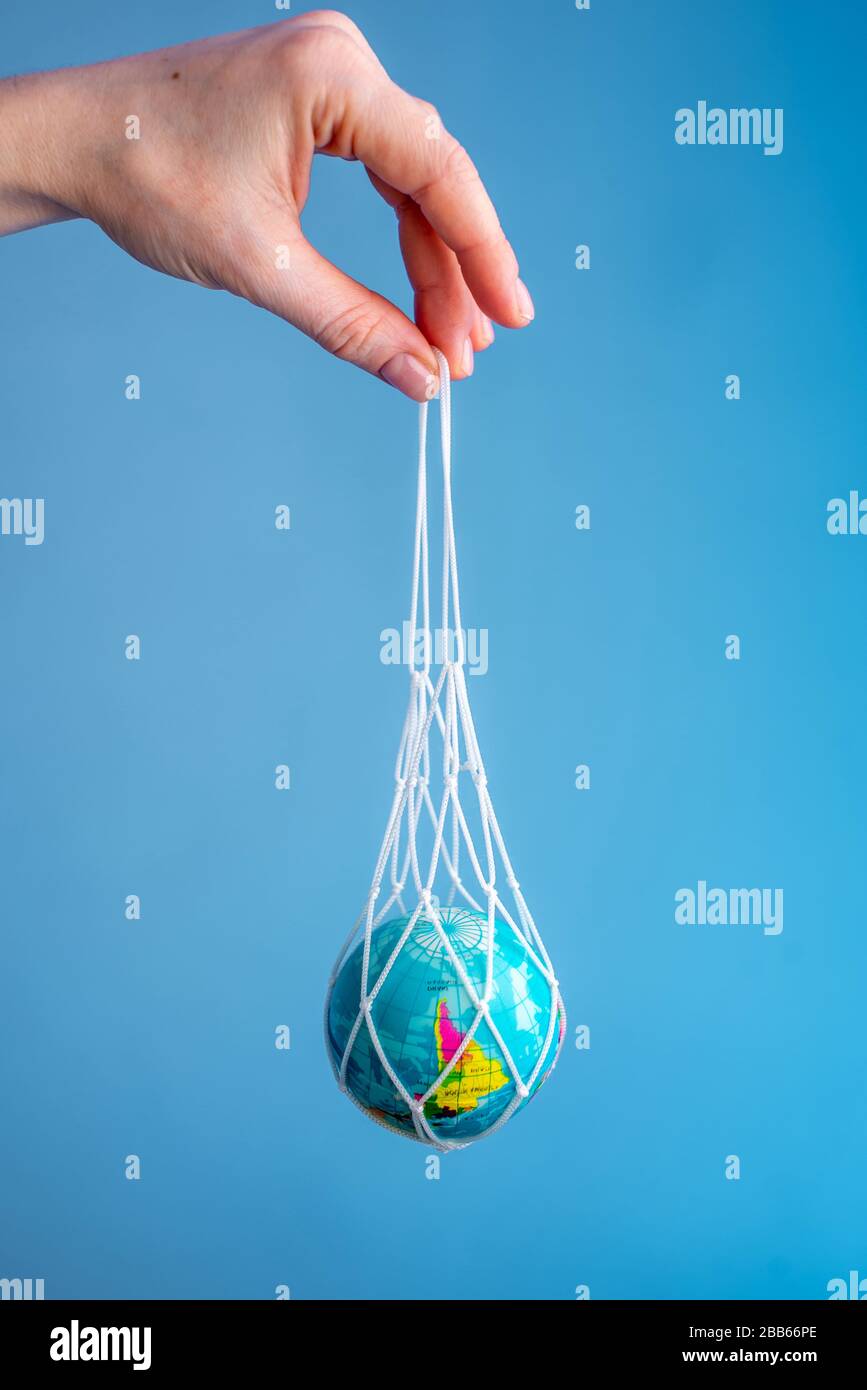 Hand holding a string bag with the planet Earth inside on a blue ...