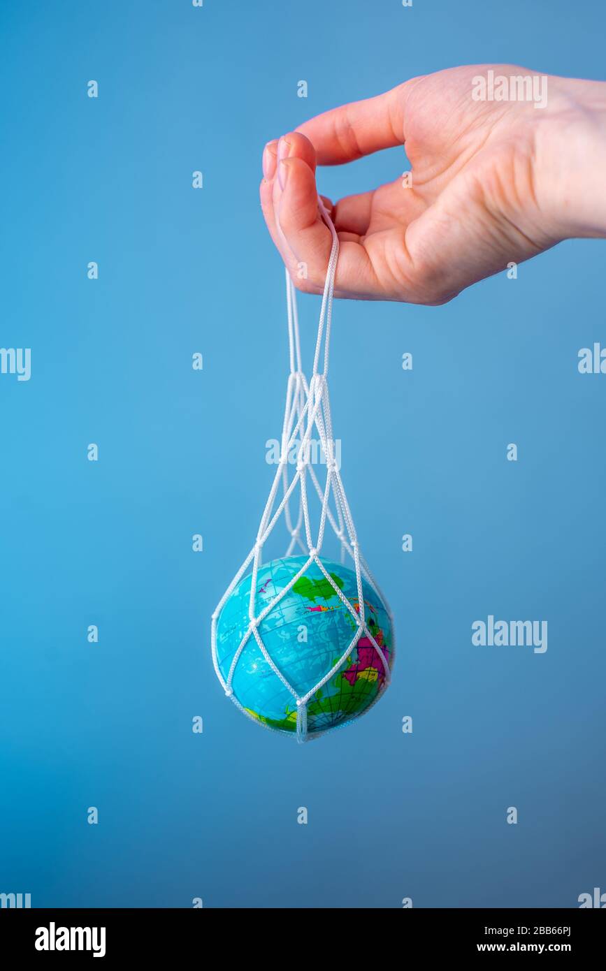 Hand holding a string bag with the planet Earth inside on a blue ...