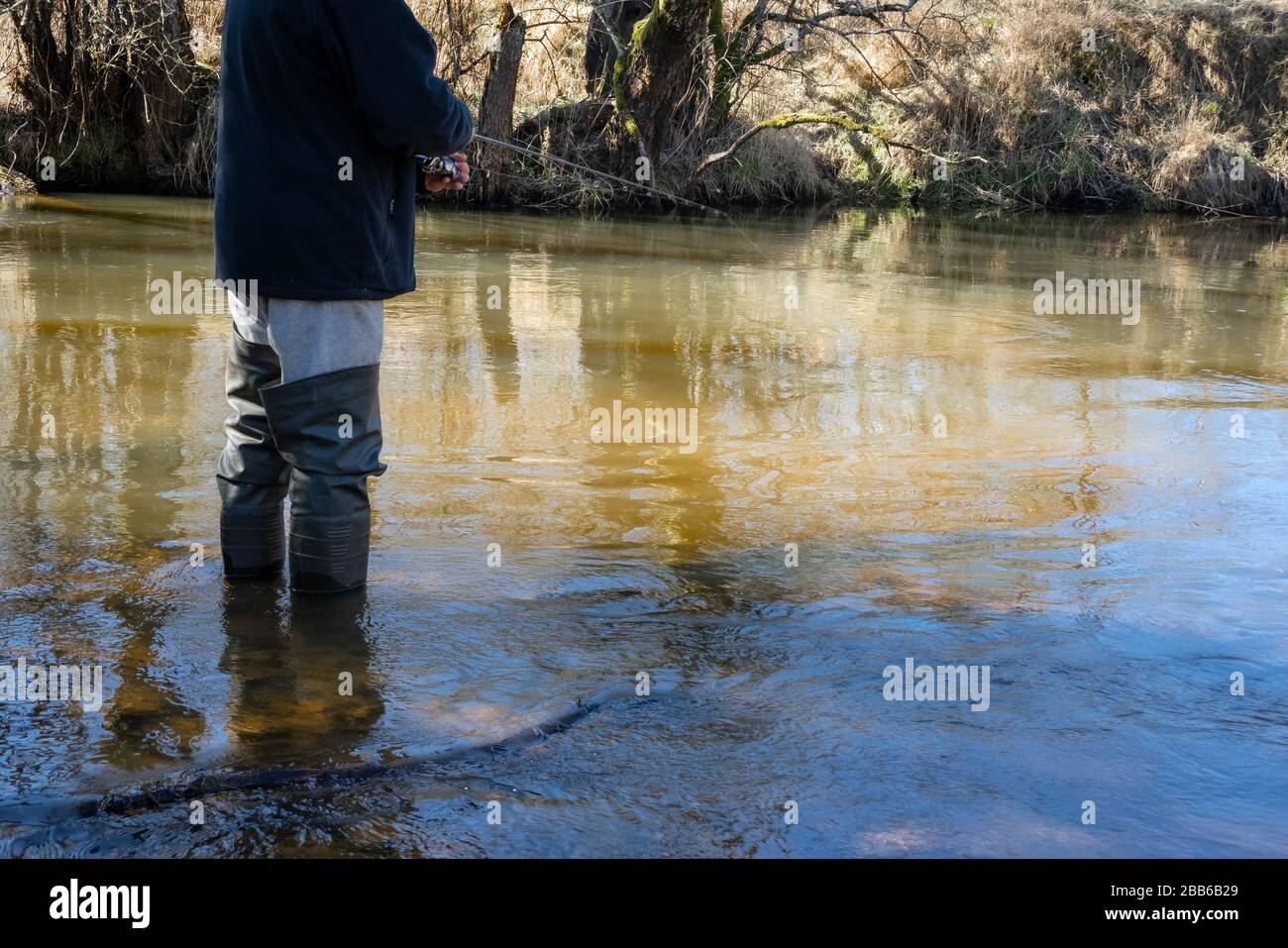 Fisherman with rubber boots trout fishing in a creek on a sunny day ...