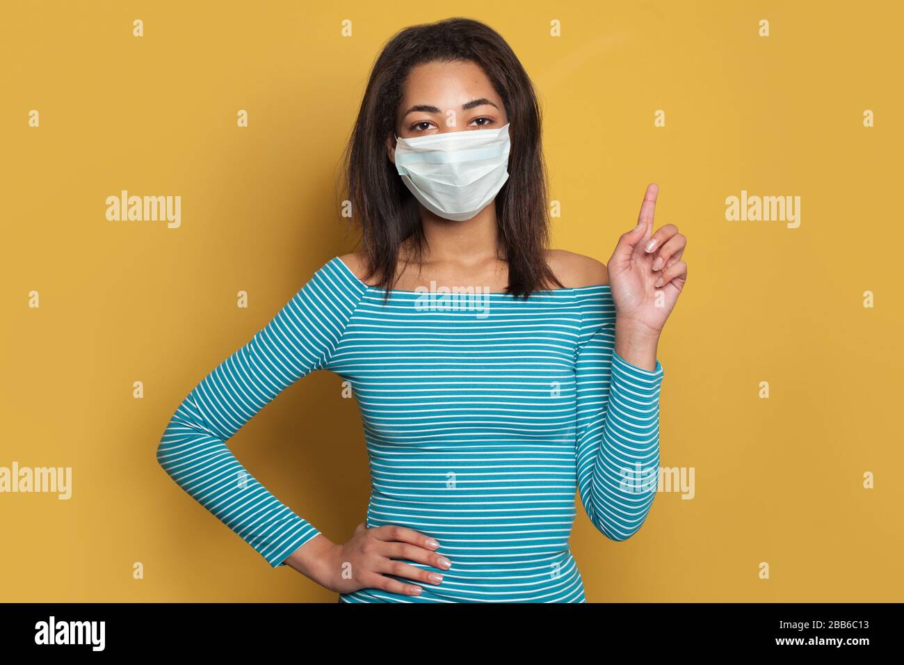 Black woman in face mask pointing up on yellow background. Flu epidemic ...