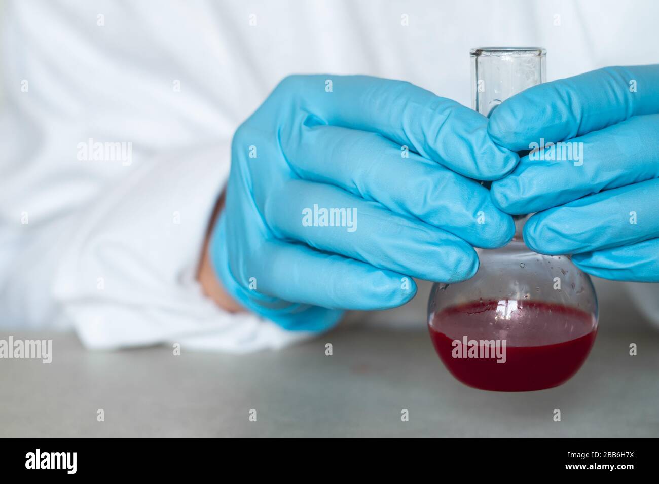 Hands of biochemist or virologist holding a flask with a blood sample ...