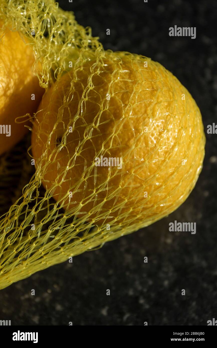 Three lemons in yellow netting against dark background, natural fruit ...