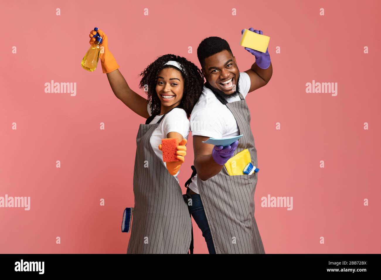 Happy african couple posing with sponges, sprayer and rag, pink ...