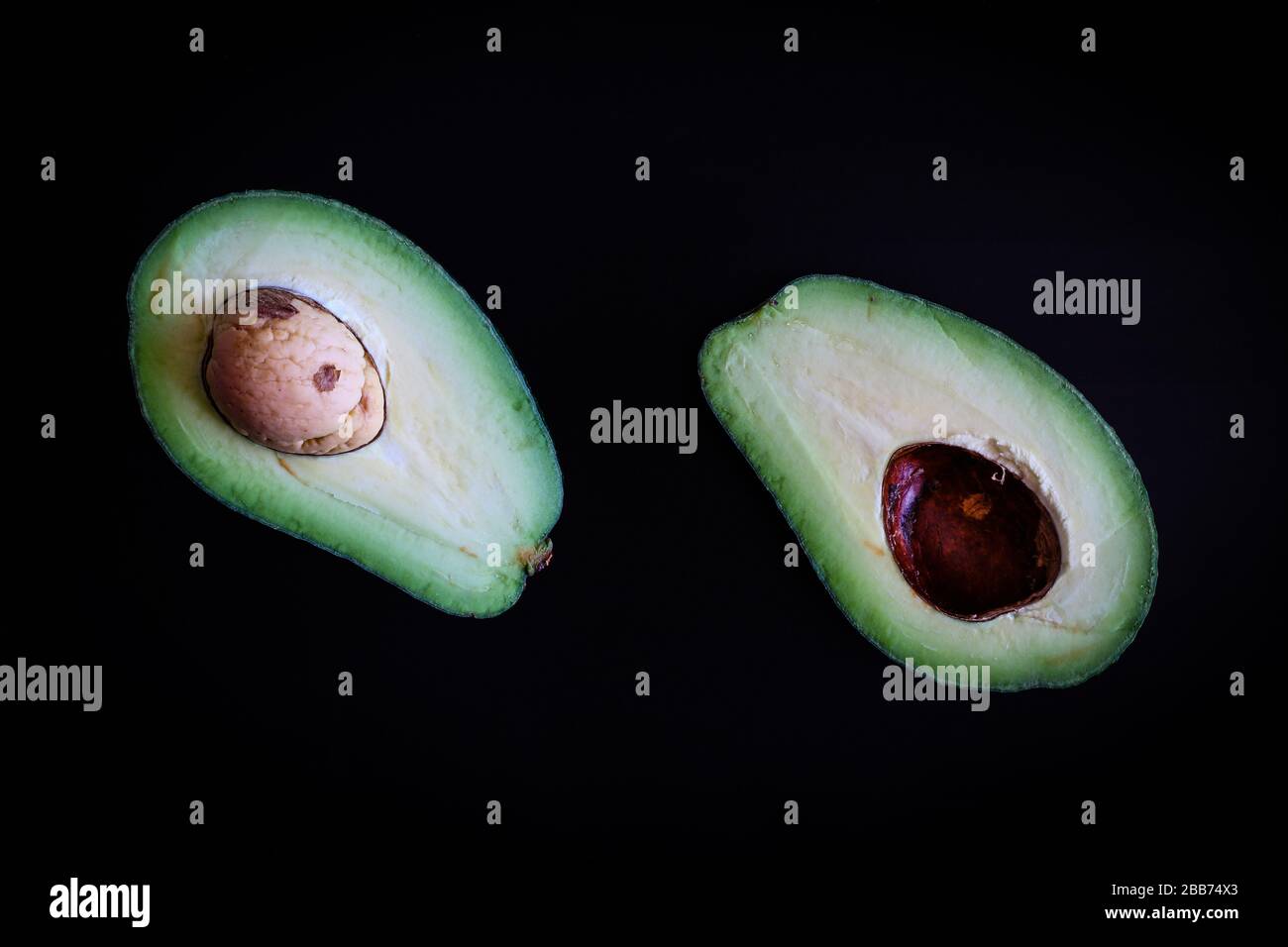 Two halves of unripe avocado arranged symmetrically against black ...