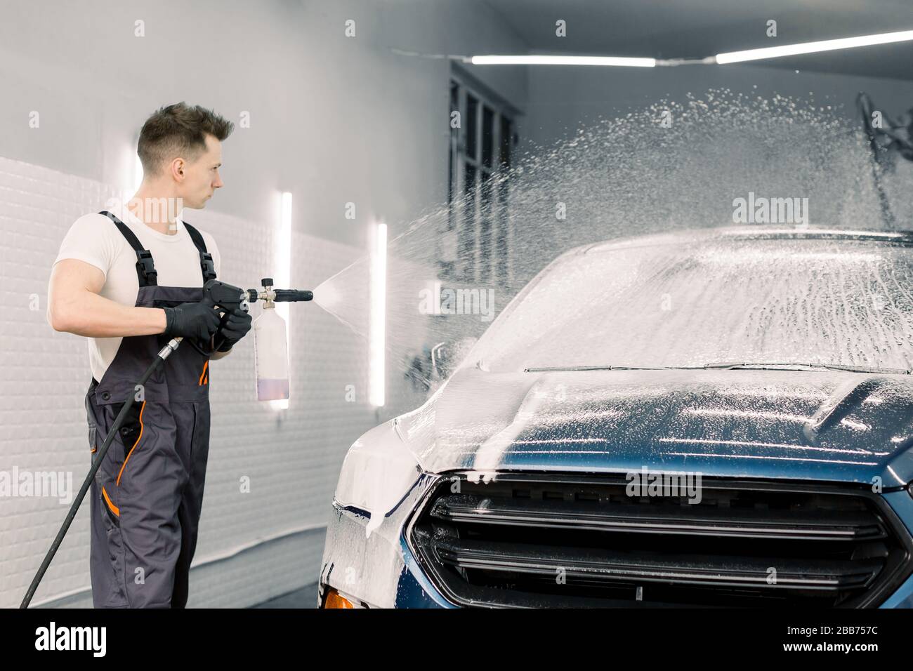 Manual car washing concept. Young man worker cleaning modern blue car ...