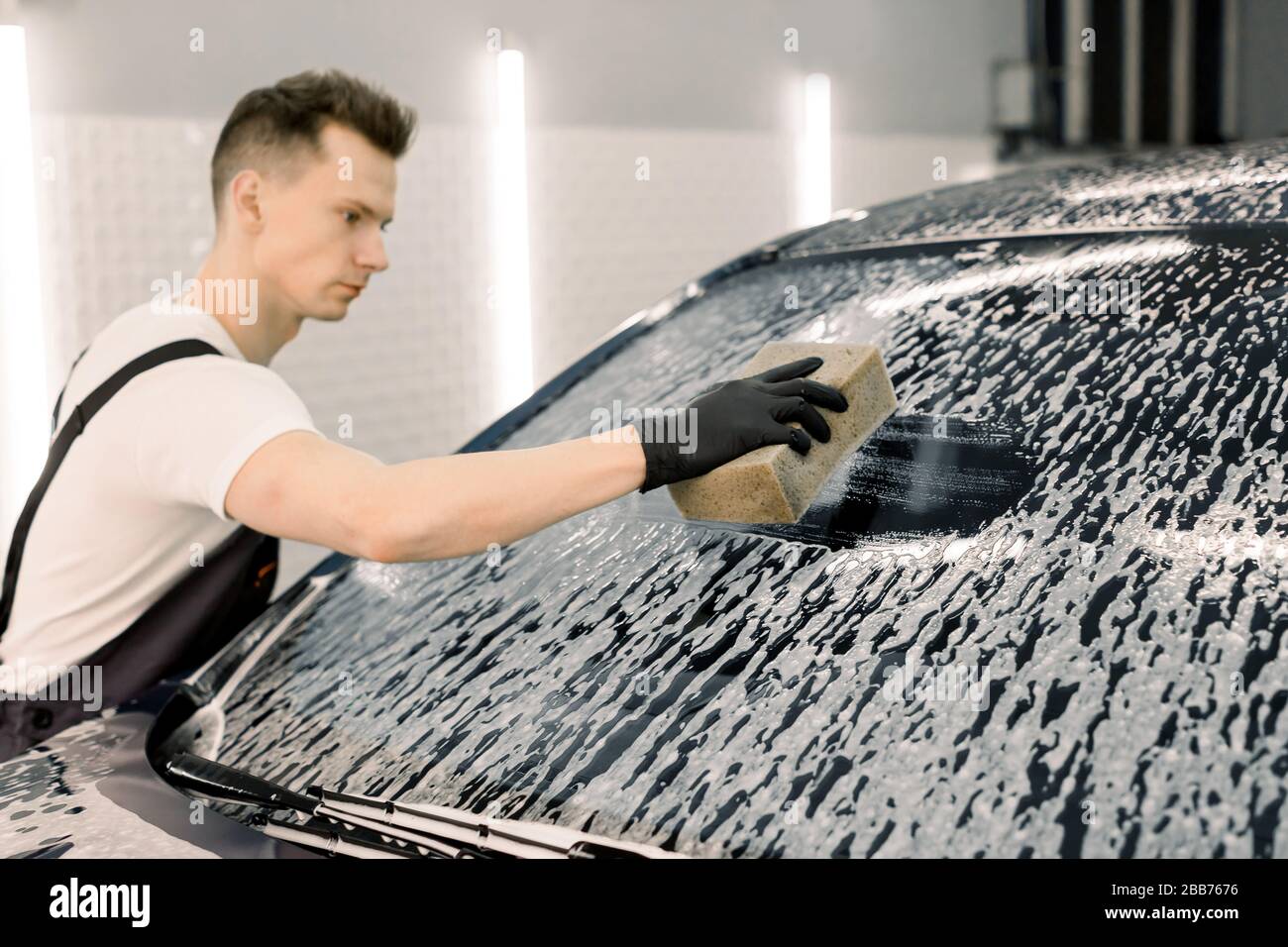 Young male car wash worker cleaning the windshield of the car with the ...