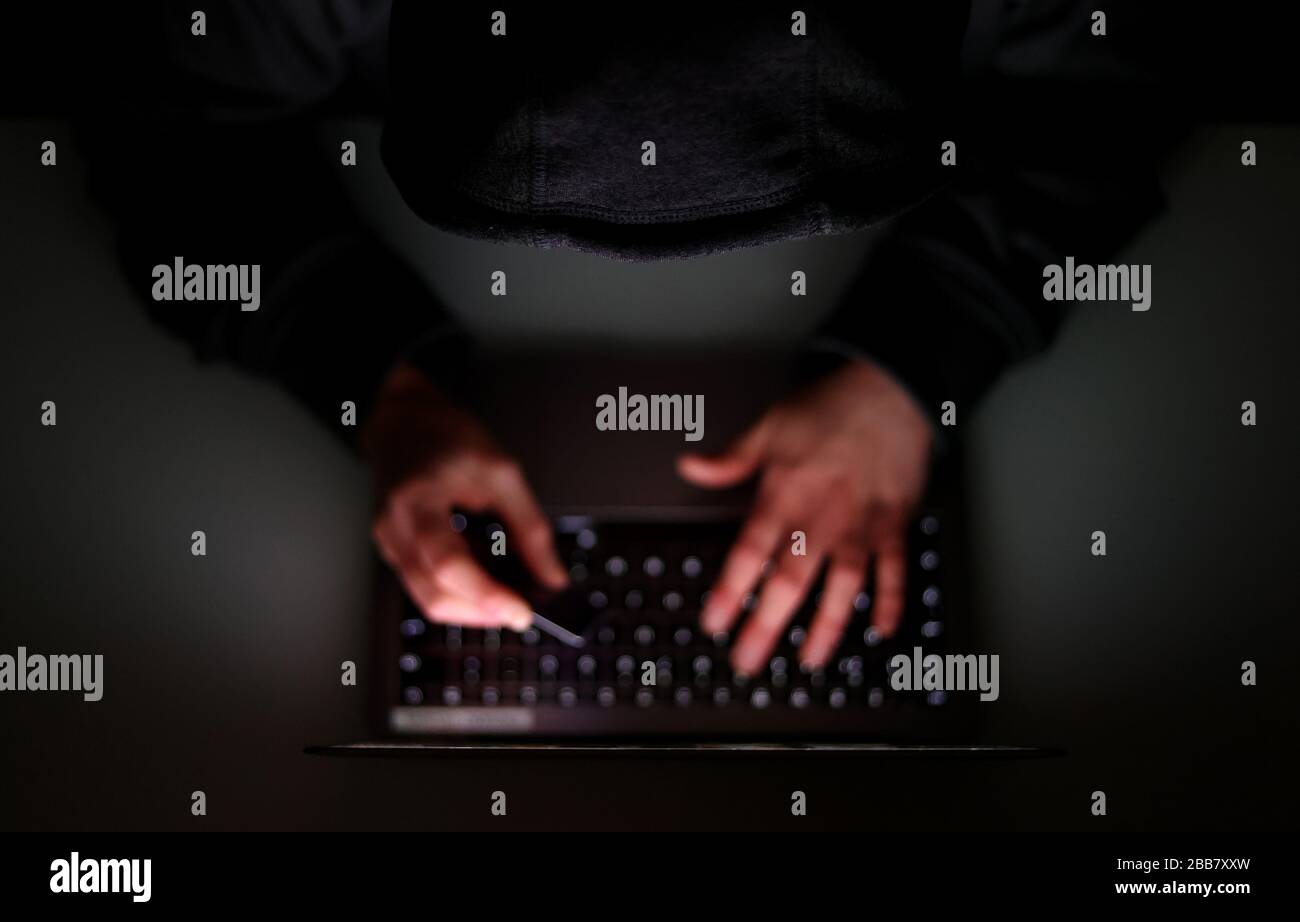 Laptop user with their hood up holding bank card hi-res stock ...