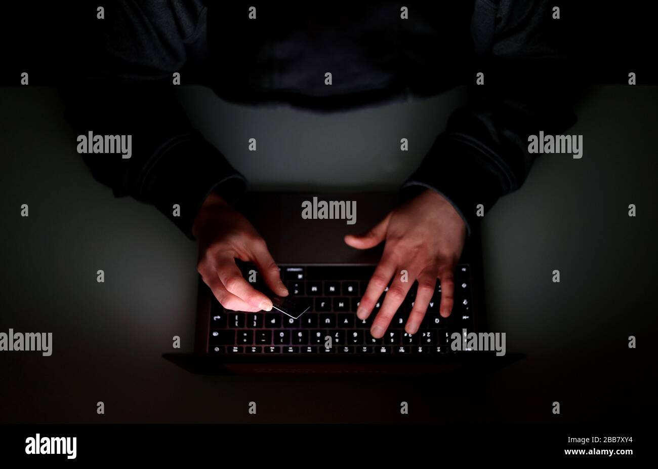 Laptop user with their hood up holding bank card hi-res stock ...