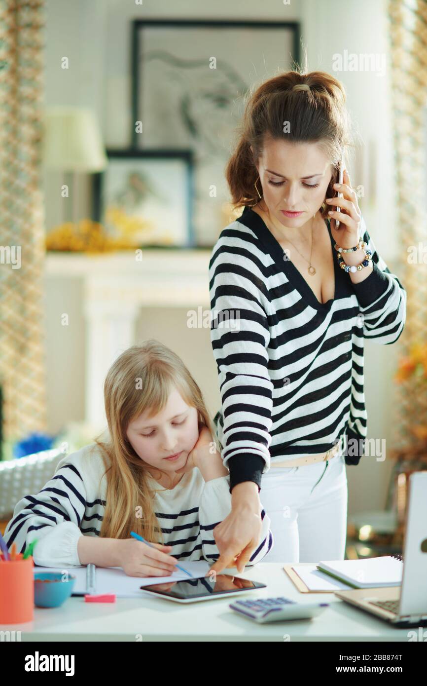 mother using a mobile phone and working and helping child with homework ...