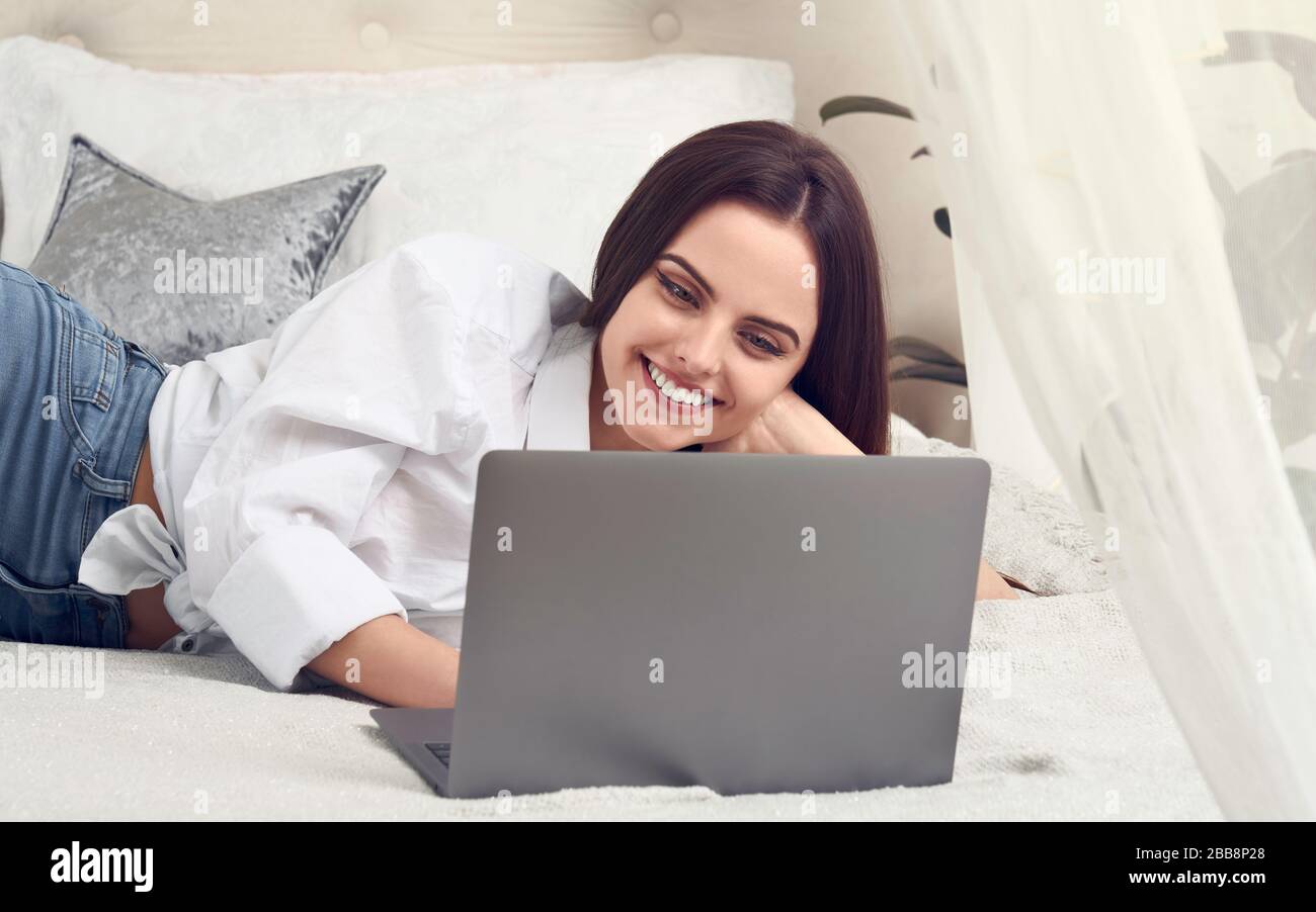 Casual young girl using laptop and smiling in bed. Girl smiling in ...