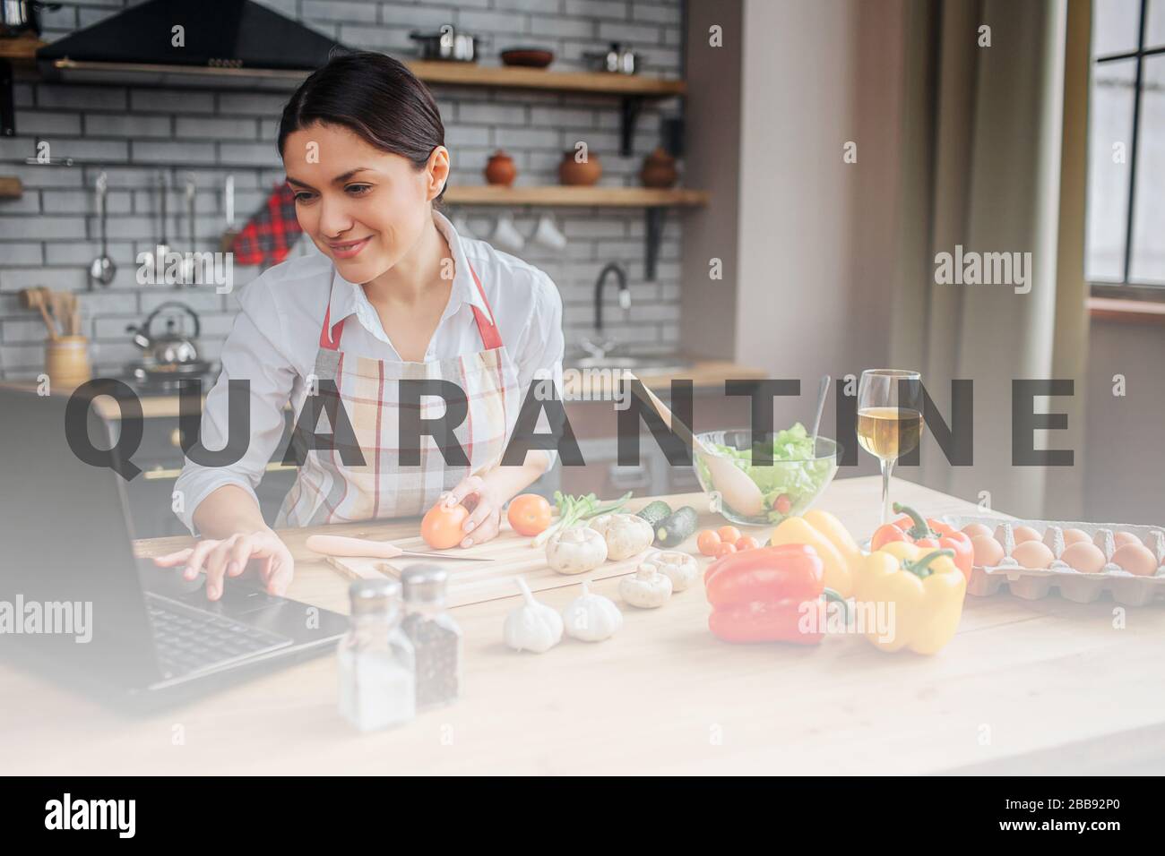 Cheerful adult woman sit at table in kitchen. She typing on keyboard ...