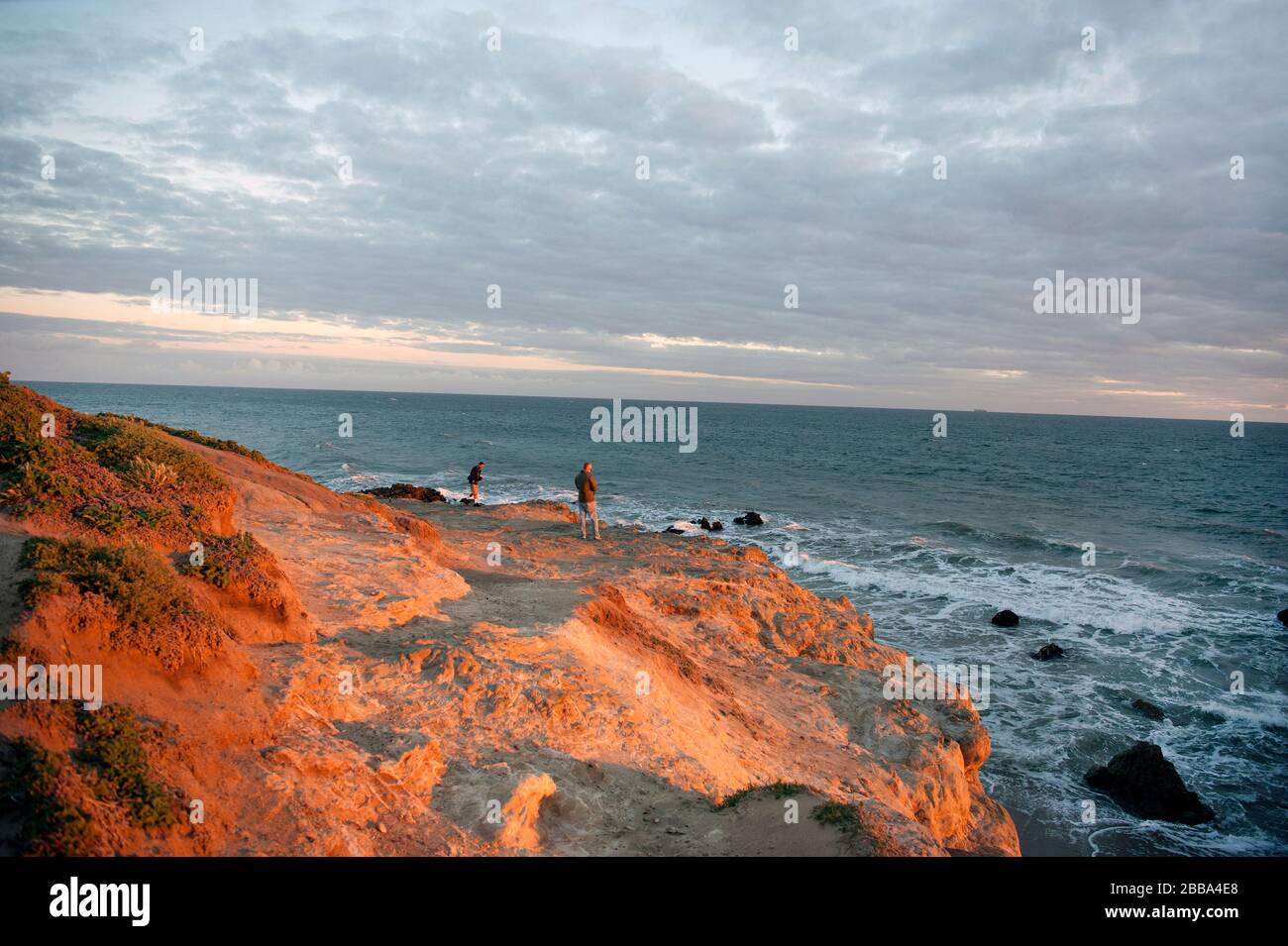 People standing on cliffs above the Pacific Ocean at Malibu at sunset ...