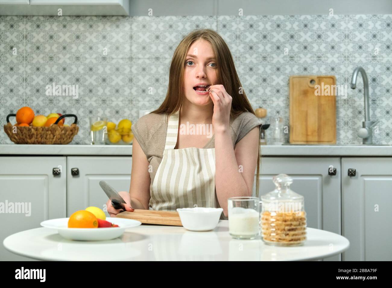Young woman sitting in kitchen with fruit products knife cutting board ...