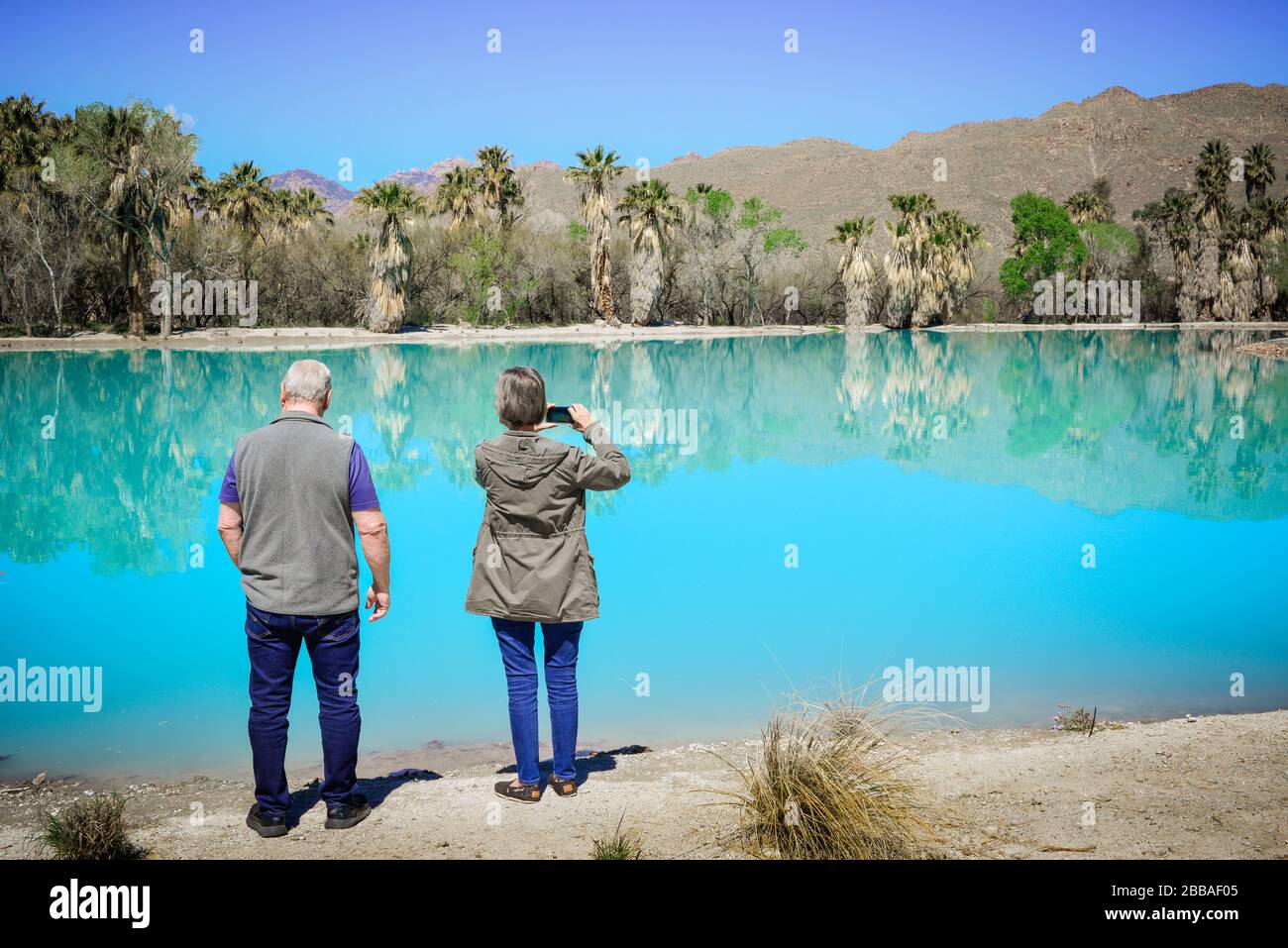 An older couple take cellphone photos of the aqua blue pond created by ...