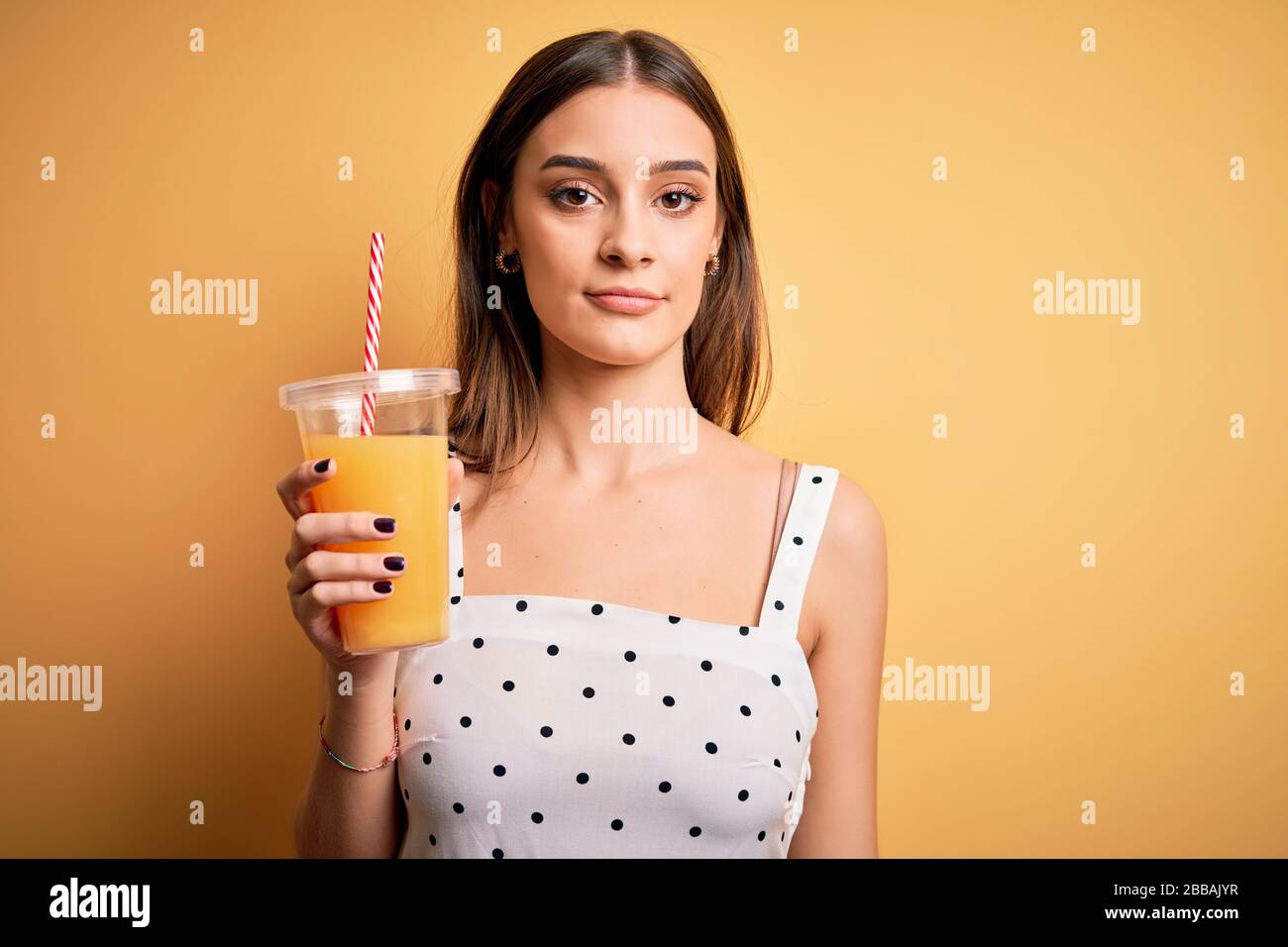 Young beautiful brunette woman drinking healthy orange juice over ...