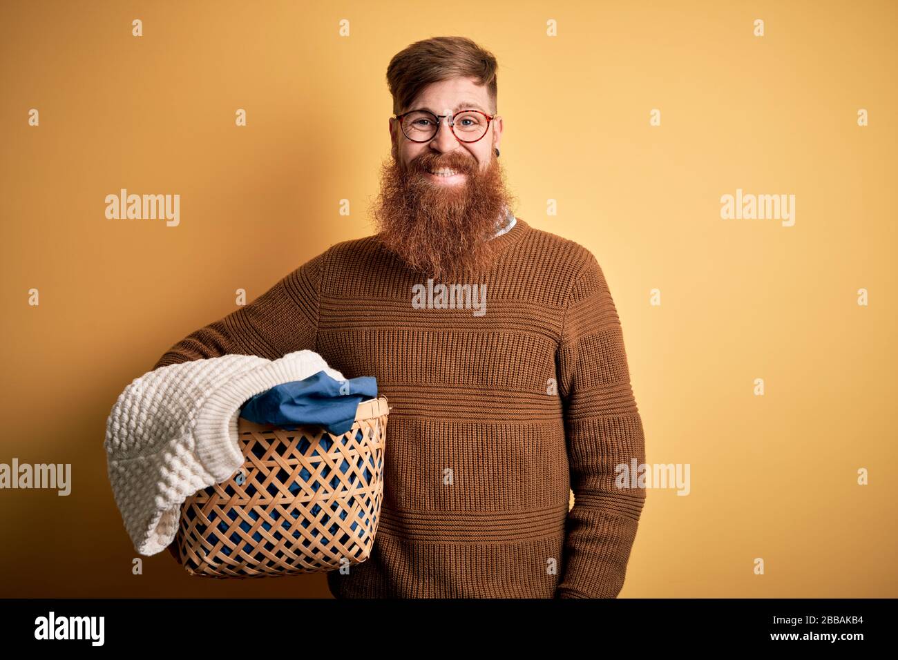 Redhead Irish Man With Beard Doing Housework Laundry Over Yellow Background With A Happy Face