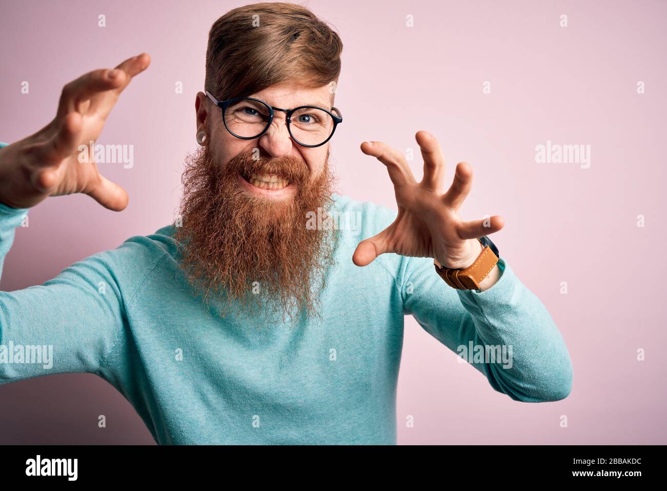 Handsome Irish redhead man with beard wearing glasses over pink ...