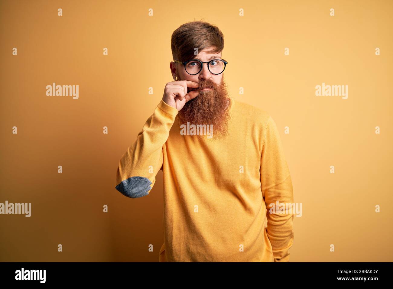 Handsome Irish redhead man with beard wearing glasses over yellow ...