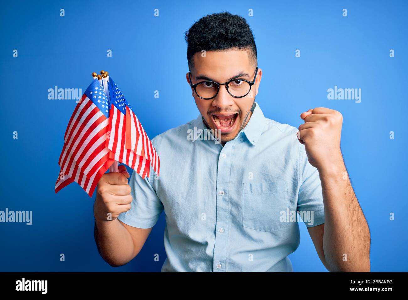 Young handsome patriotic man holding united states flags celebrating ...