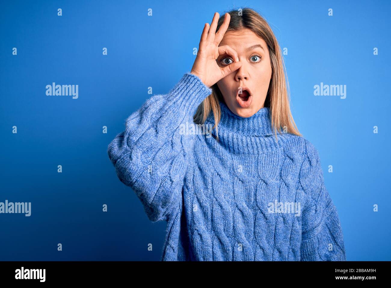 Young beautiful blonde woman wearing winter wool sweater over blue ...
