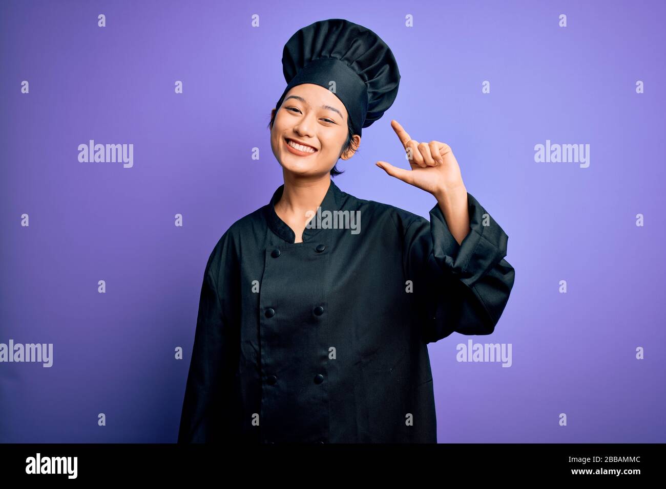 Young beautiful chinese chef woman wearing cooker uniform and hat over ...
