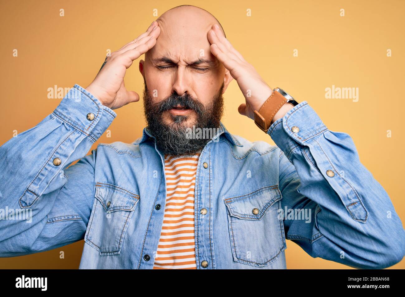Handsome bald man with beard wearing casual denim jacket and striped t ...