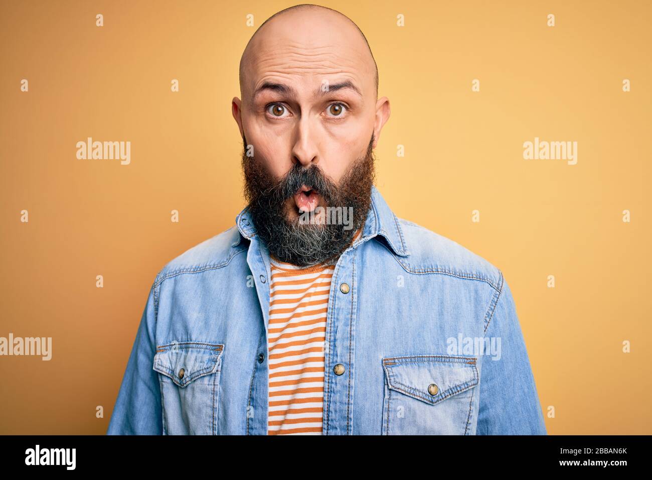 Handsome bald man with beard wearing casual denim jacket and striped t ...