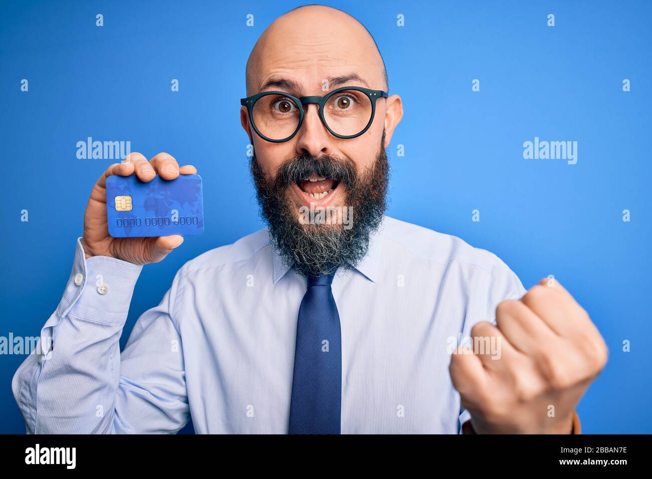 Handsome bald business man with beard holding credit card over isolated ...