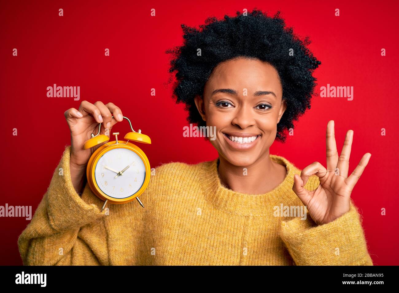 Young African American afro woman with curly hair holding vintage alarm ...