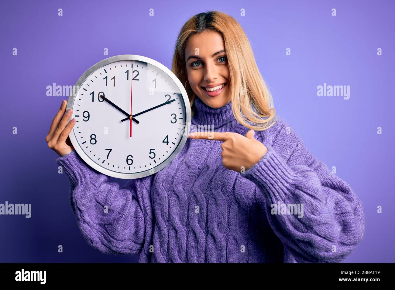 Young beautiful blonde woman doing countdown holding big clock over ...