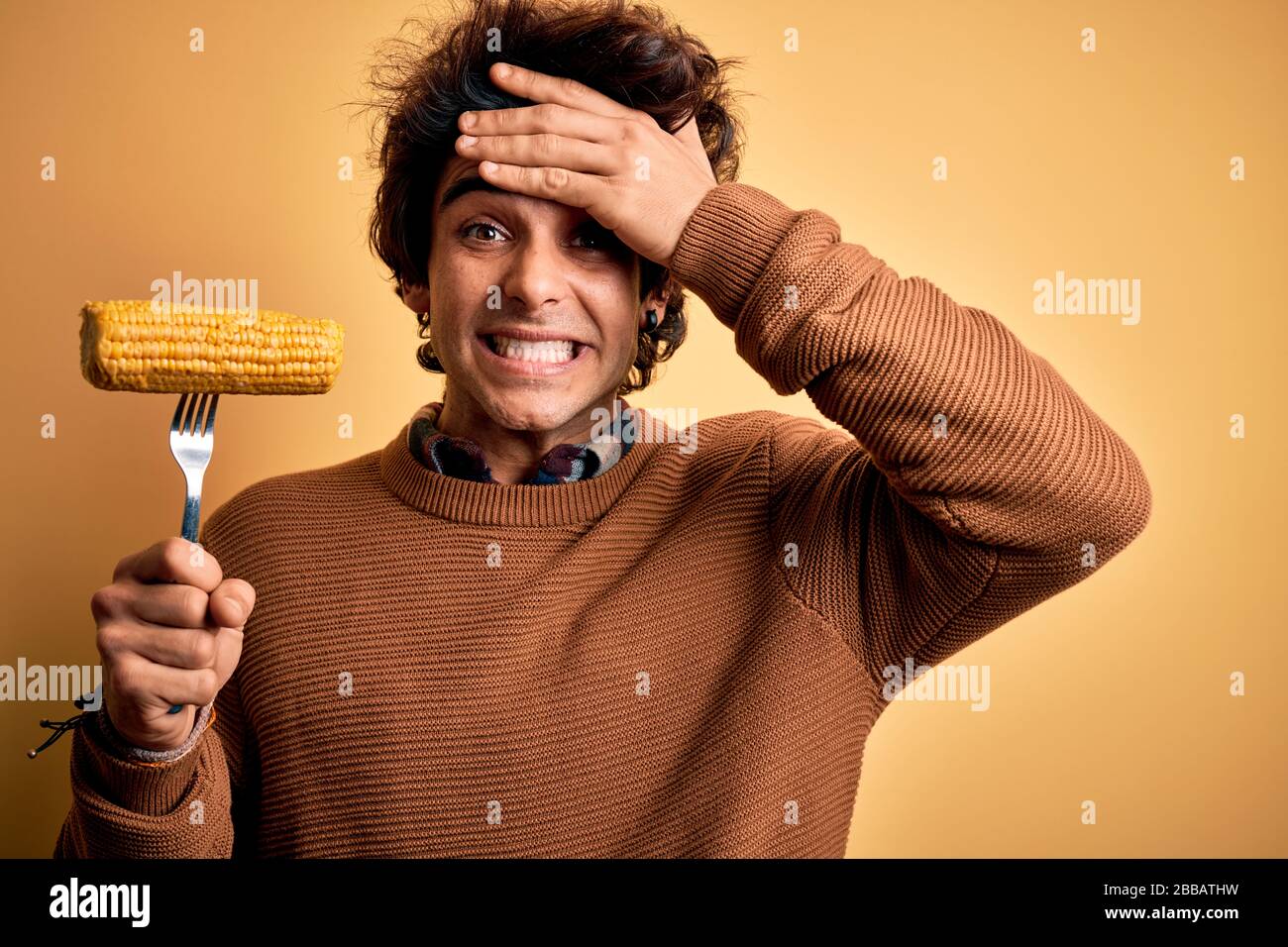 Young handsome man holding fork with cob corn standing over isolated ...
