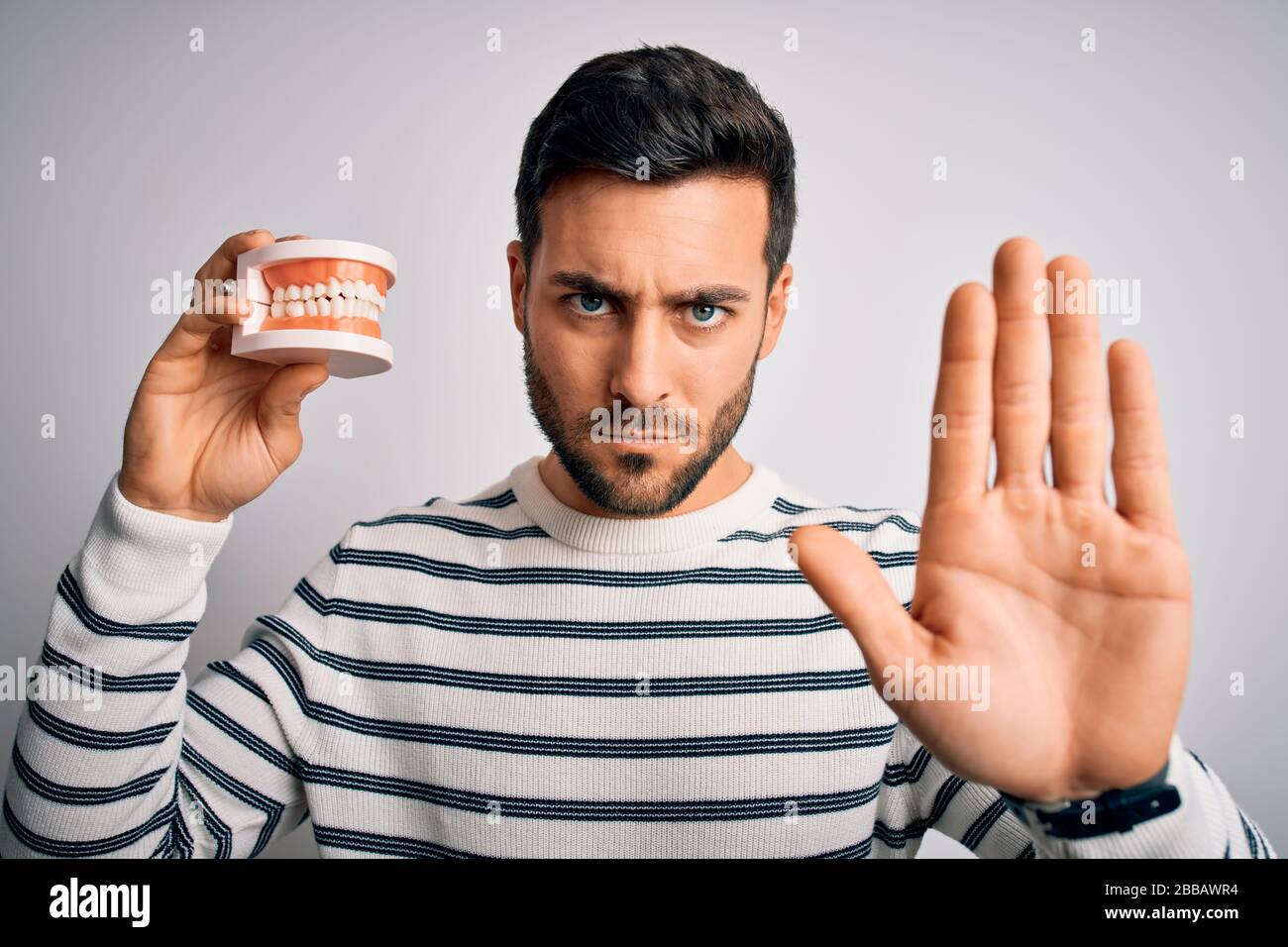 Young handsome man with beard holding plastic denture teeth over white ...