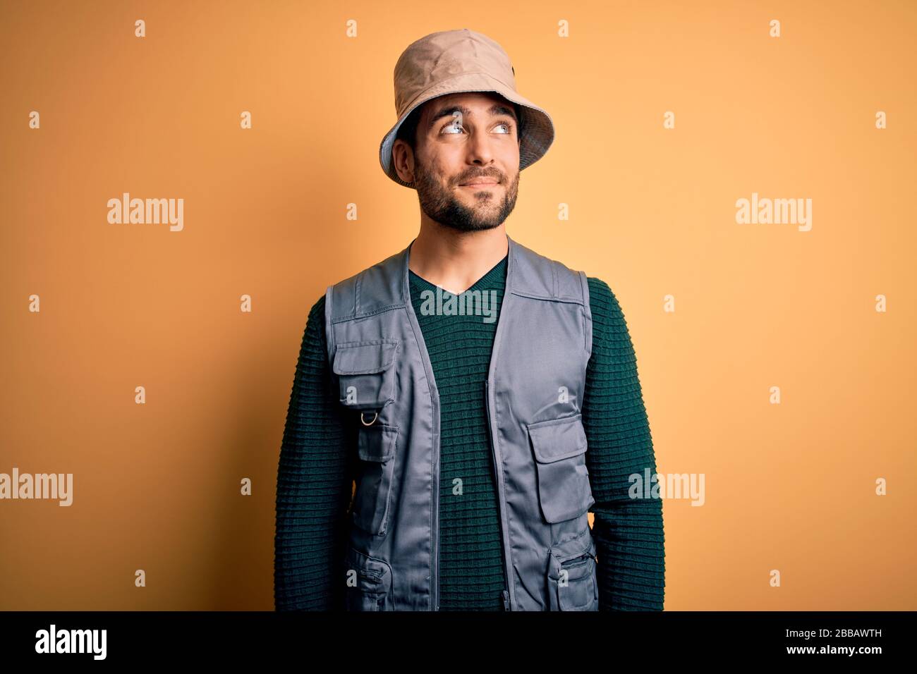 Handsome tourist man with beard on vacation wearing explorer hat over ...