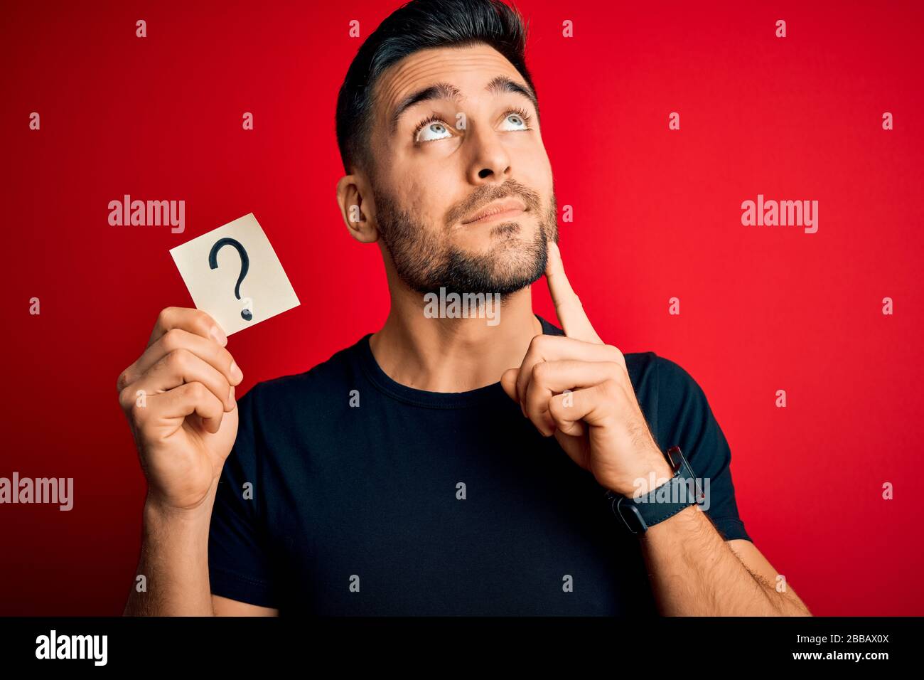 Young handsome man holding paper with question mark symbol over red ...