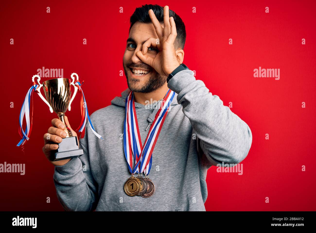 Young handsome succesful man holding trophy wearing medals over red ...