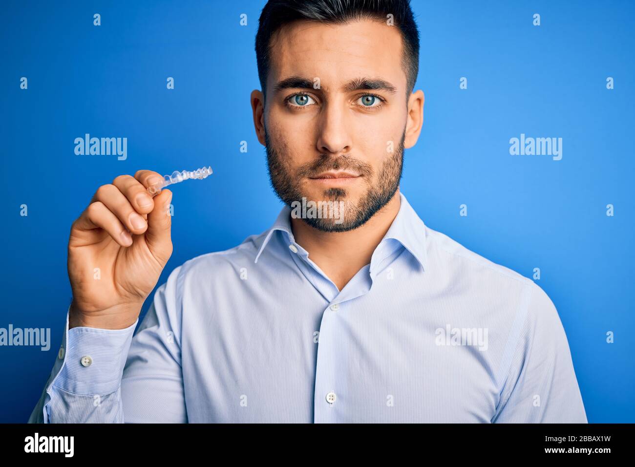 Young handsome man holding dental aligner tooth correction over blue ...