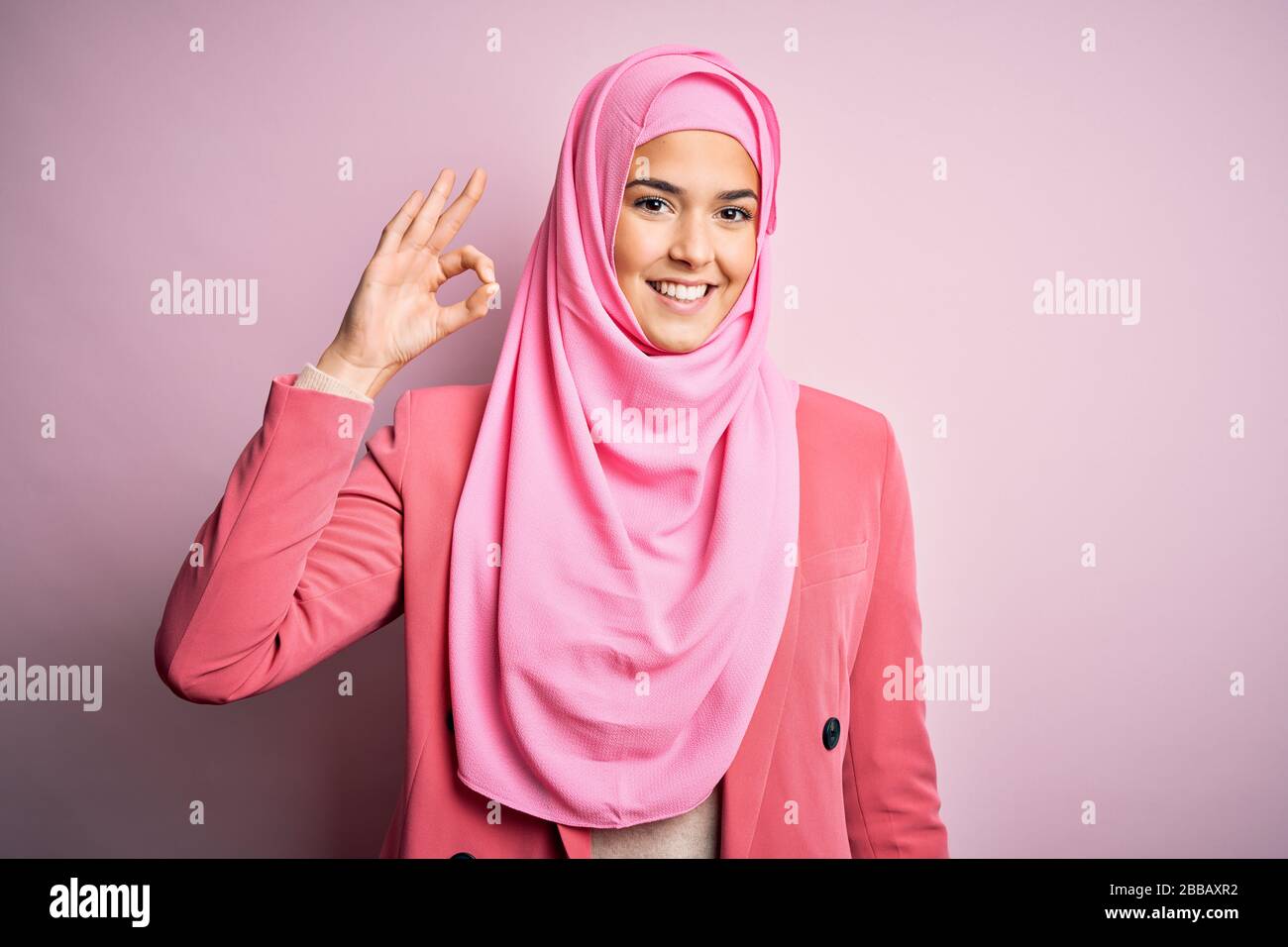 Young beautiful girl wearing muslim hijab standing over isolated pink ...