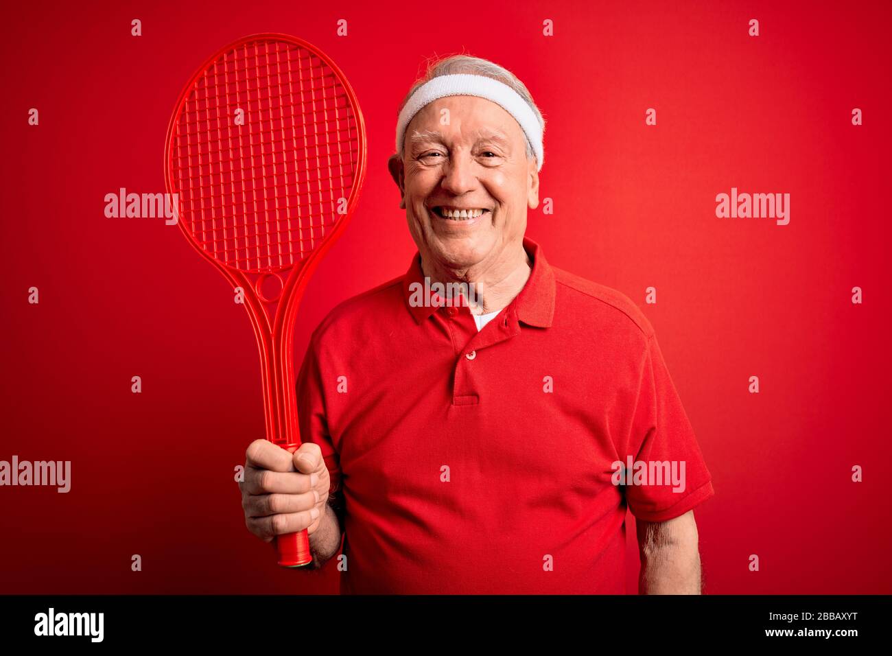 Grey haired senior tennis player man holding racket over red isolated ...