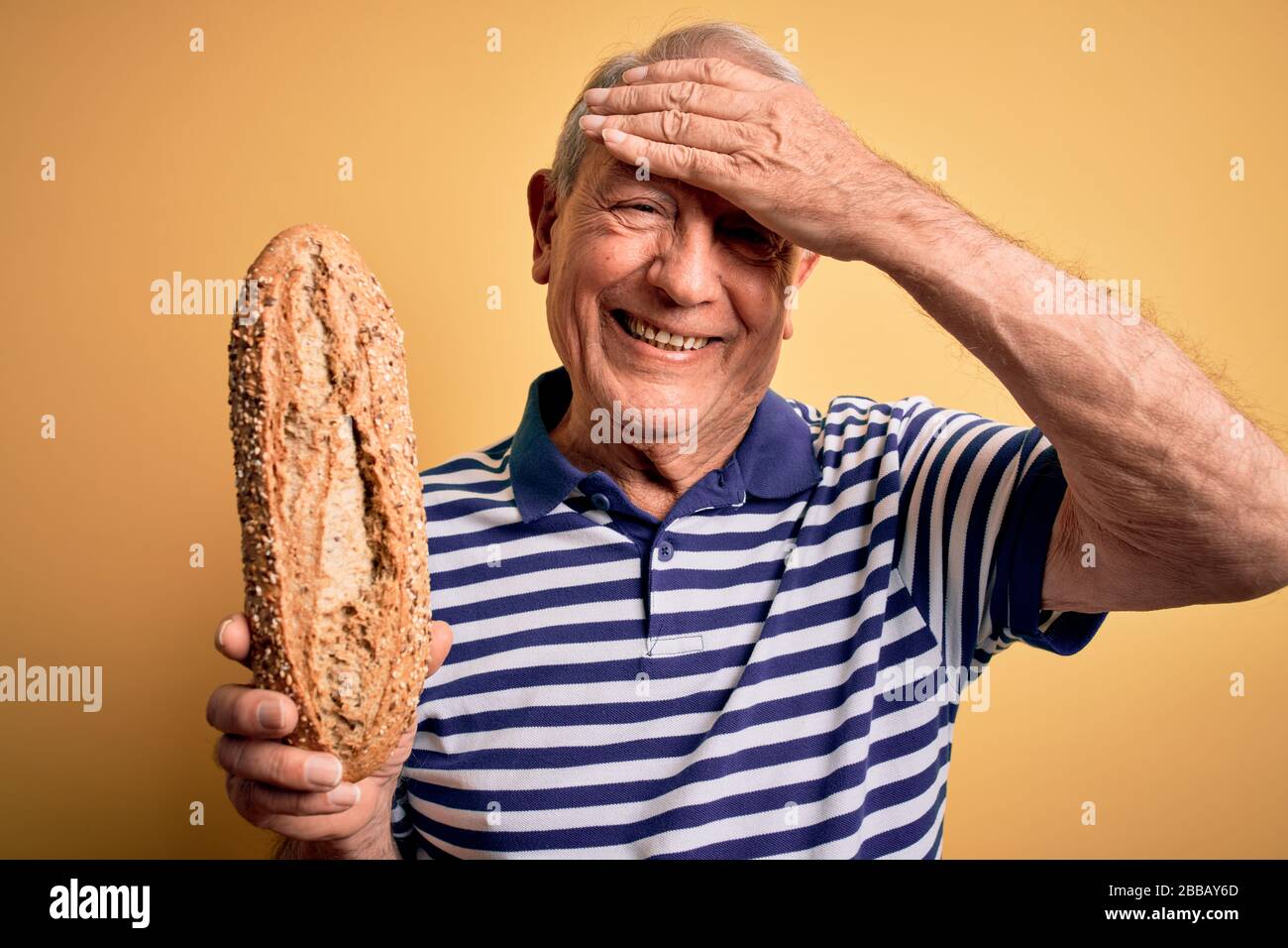 Grey haired senior man holding healthy wholemeal bread over yellow ...