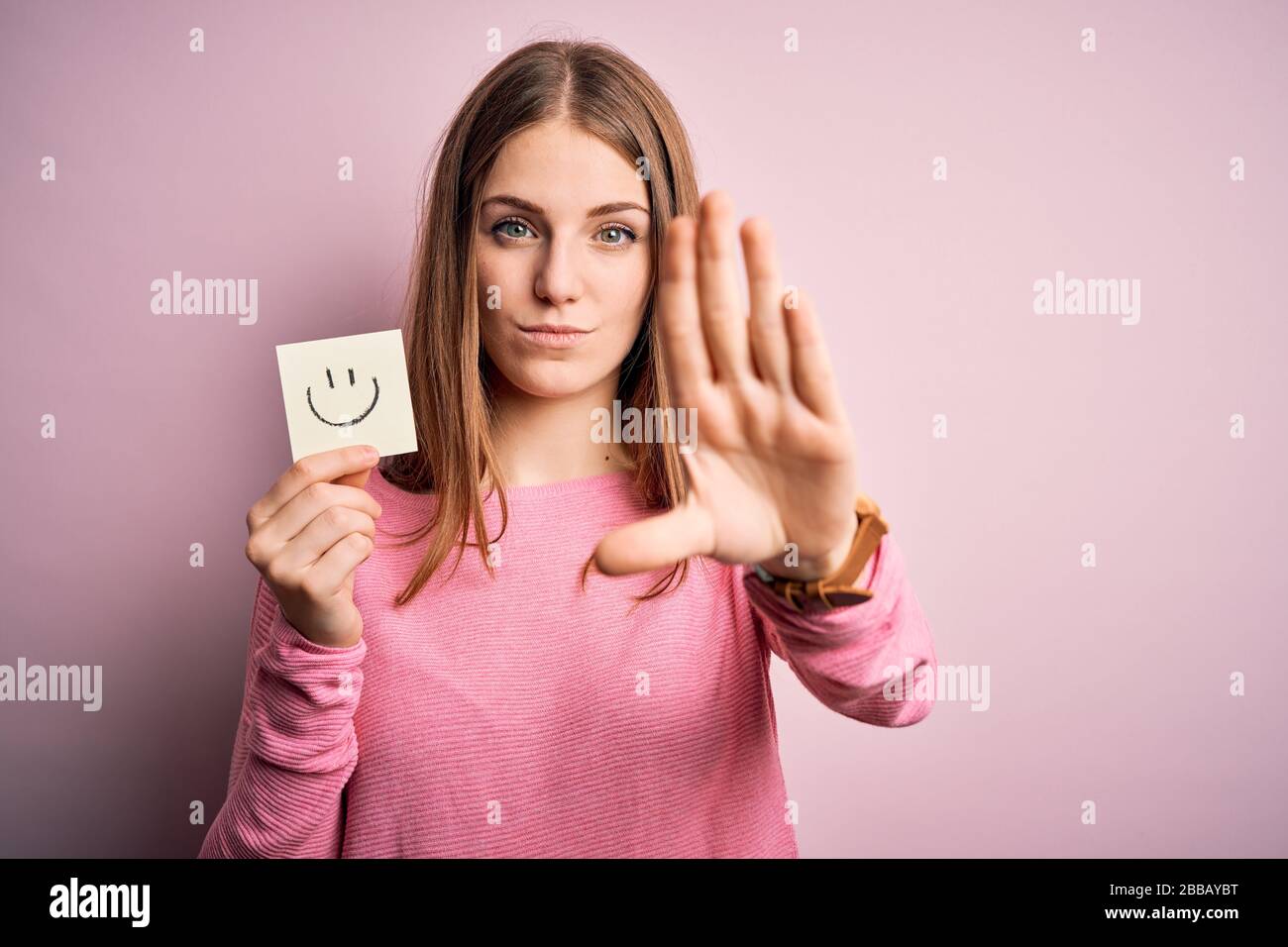 Young beautiful redhead woman holding reminder paper with smile emoji ...