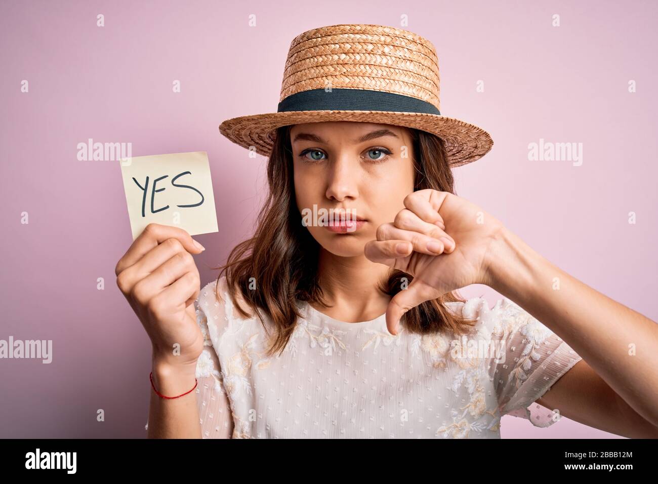 Young blonde girl wearing a hat holding paper note with yes word as ...