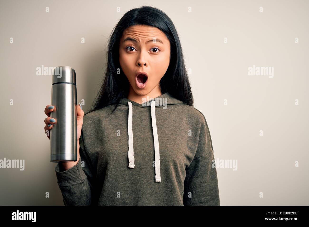 Young beautiful chinese woman holding thermo standing over isolated ...