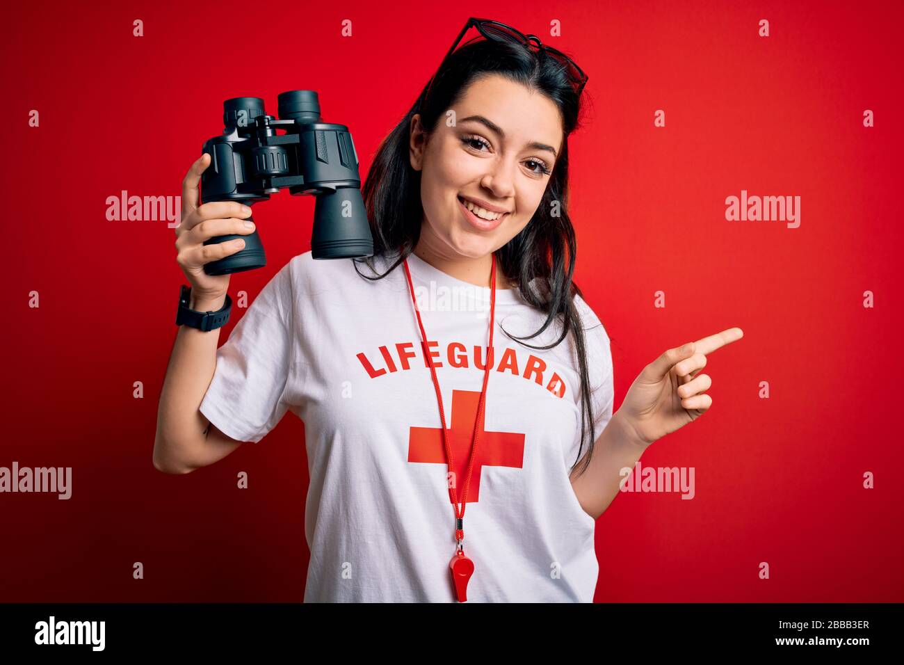 Young lifeguard woman wearing secury guard equipent holding binoculars ...