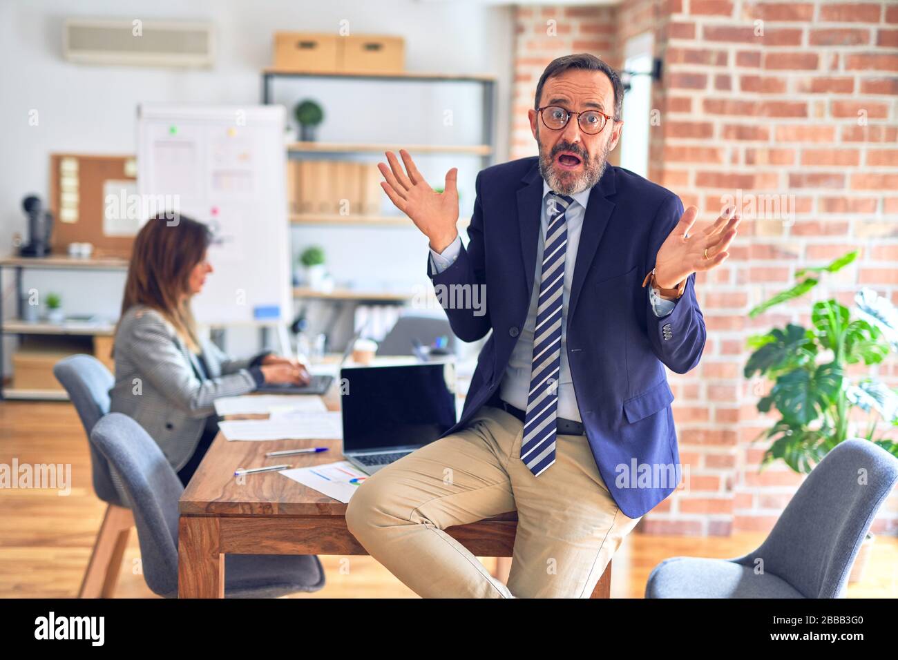 Middle age handsome businessman wearing glasses sitting on desk at the ...