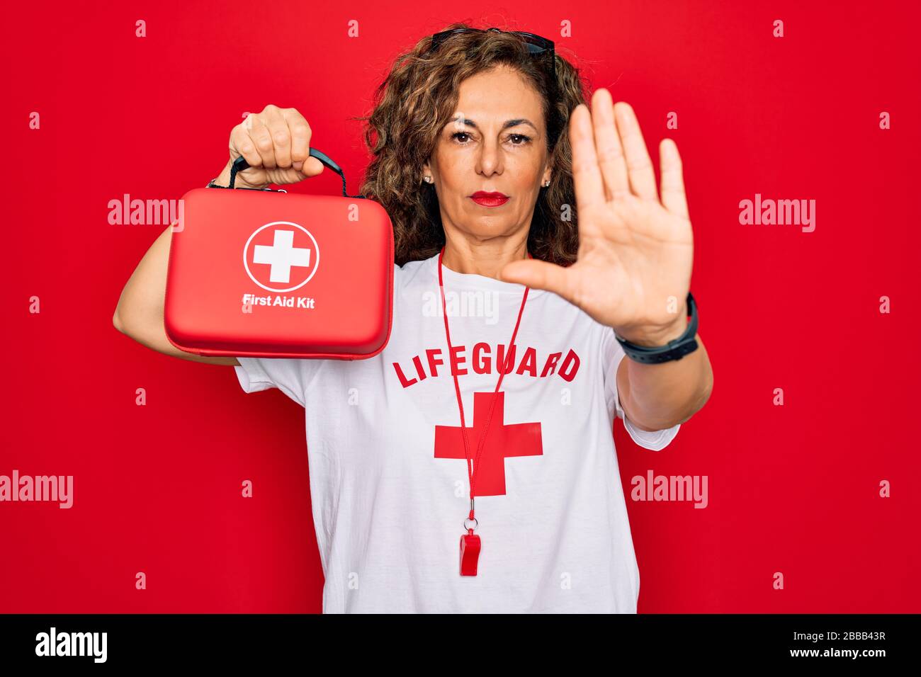 Middle age senior summer lifeguard woman holding first aid kit over red ...